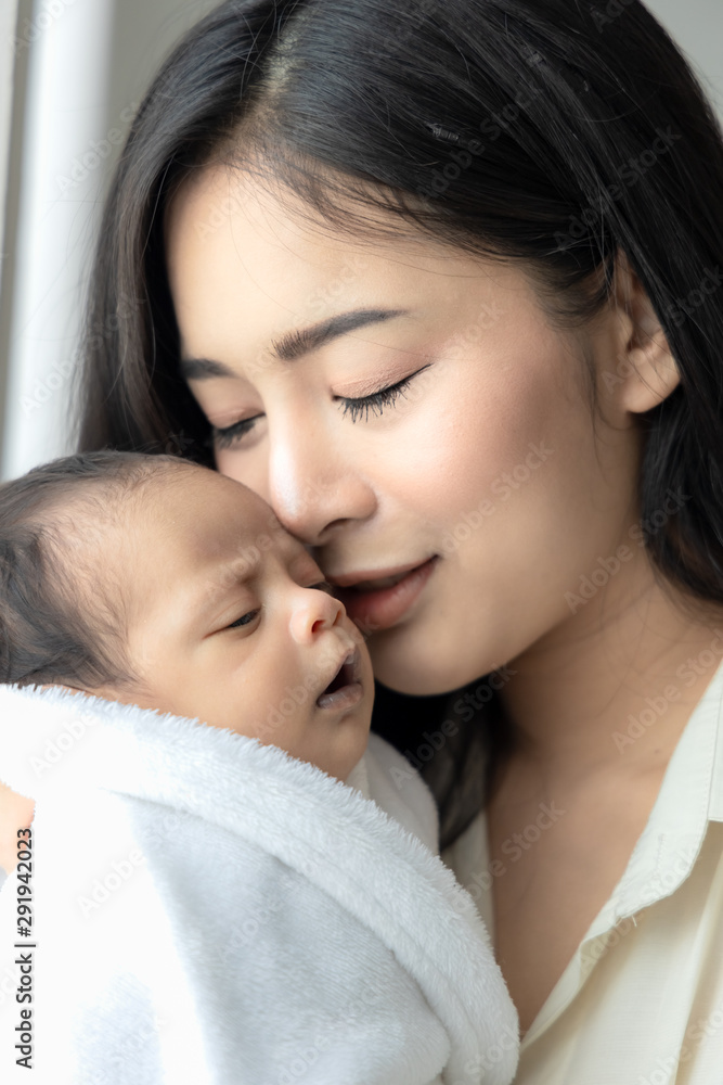 Close up asian young mother hugging and kissing her cute newborn baby. Wife and mother's day ...