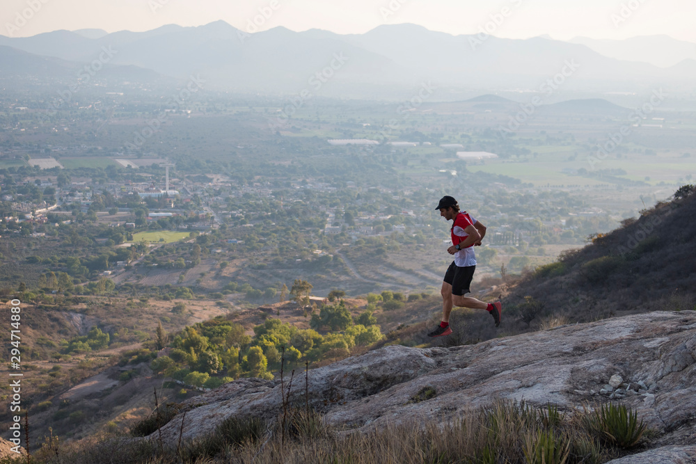 Athletic male trail runner running down rocky terrain at sunset, el ...
