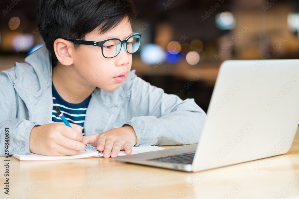 Smart looking Asian preteen boy writing and using computer laptop ...