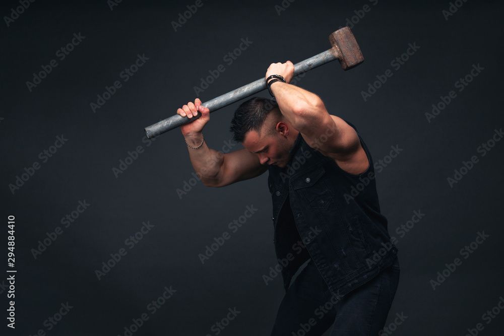 young bodybuilder in black clothes with a sledgehammer in his hands ...