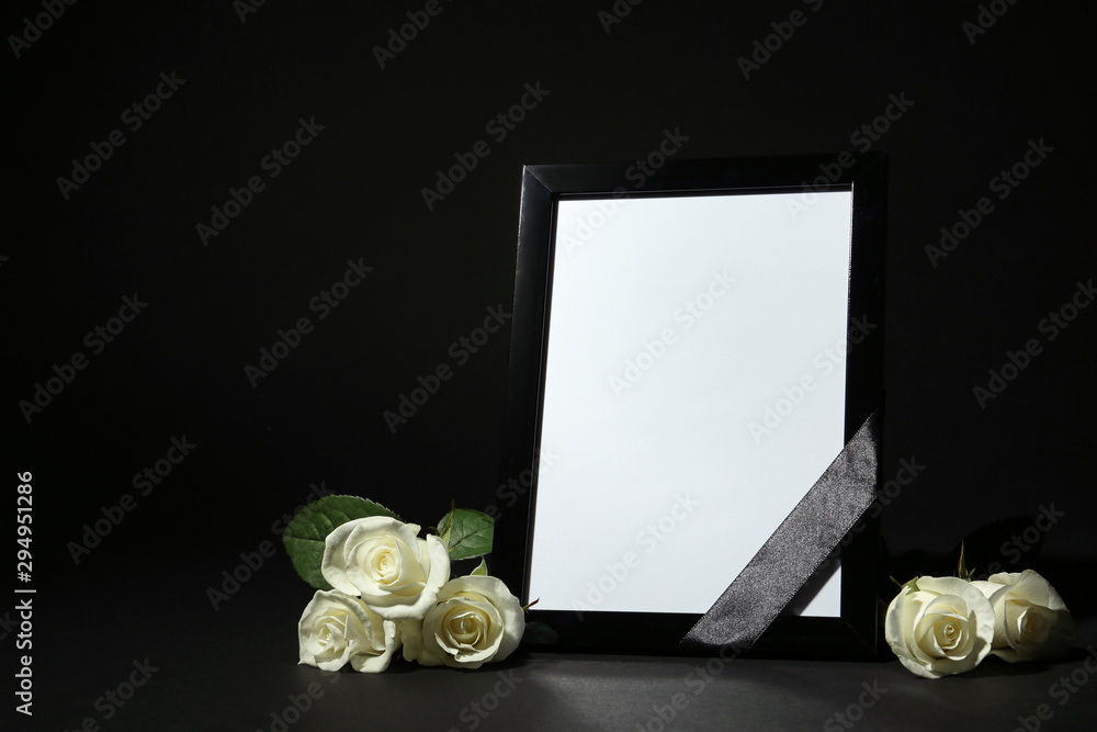 Funeral photo frame with ribbon and white roses on dark table against ...