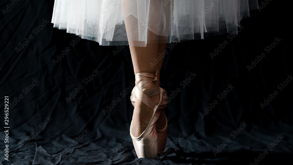 Close-up of dancing legs of ballerina wearing white pointe on a black ...