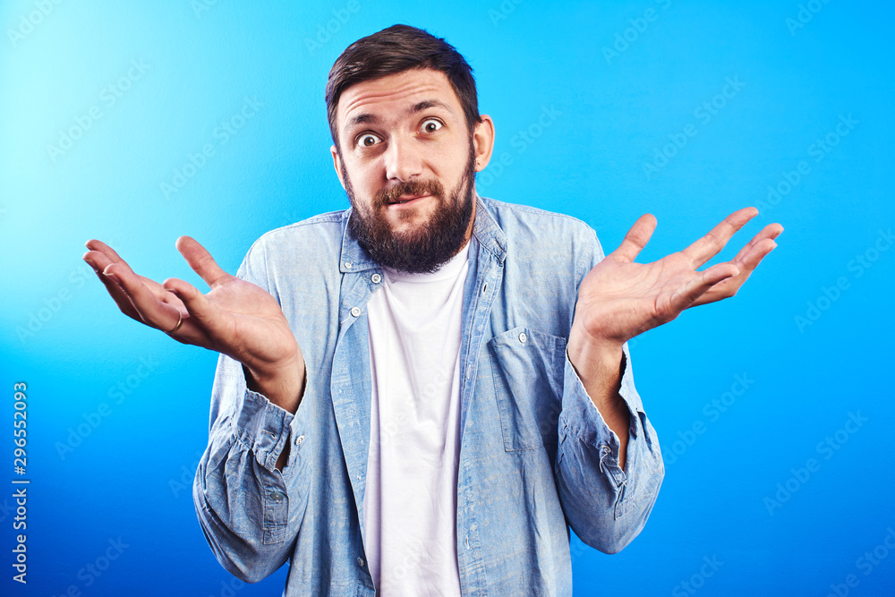 Handsome Caucasian bearded man on a blue background indifferently ...