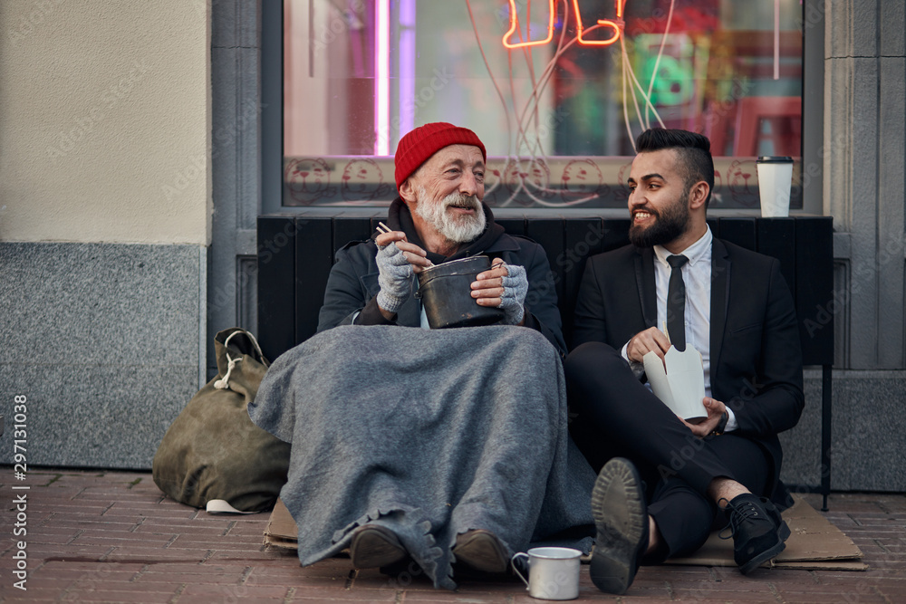 Handsome businessman in suit sitting on floor with homeless man ...