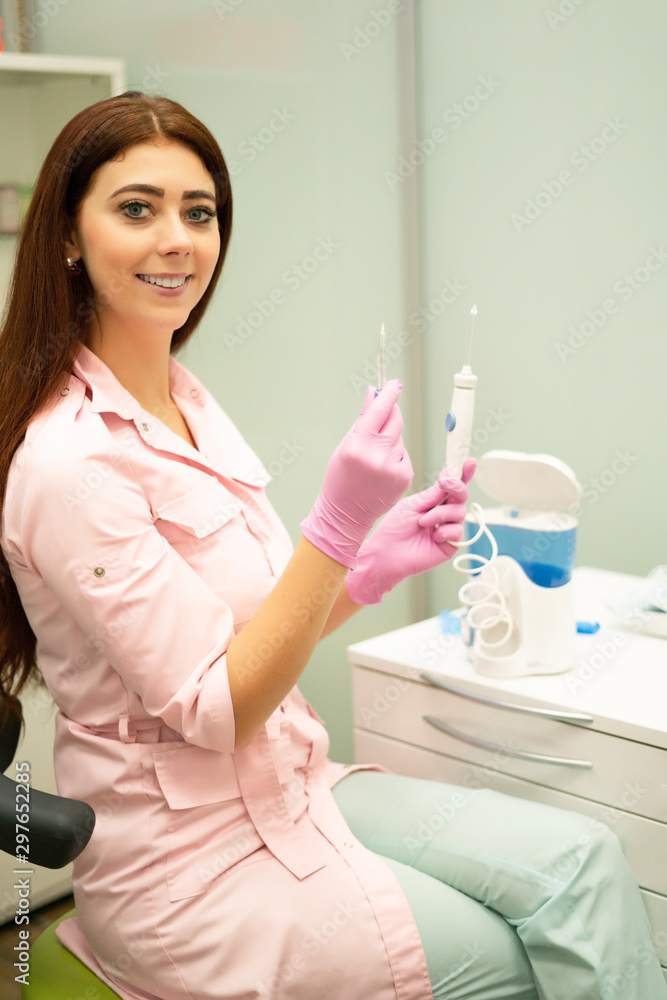 Beautiful female dentist shows irrigator work. Dentist demonstrates ...