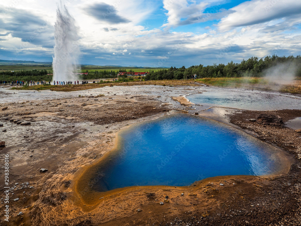 Strokkur Geyser erupting behind Blesi goethermal pool at Geysir. This ...