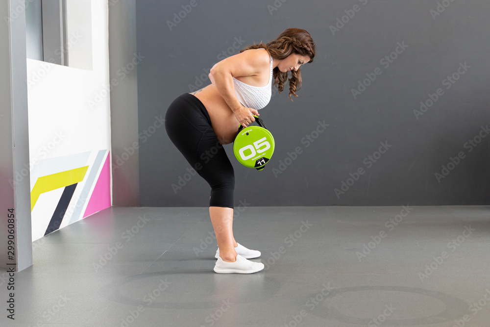 Caucasian pregnant woman in her third trimester doing bent over row ...