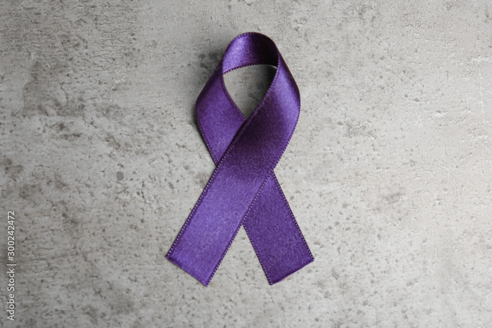 Purple ribbon on grey stone background, top view. Domestic violence ...