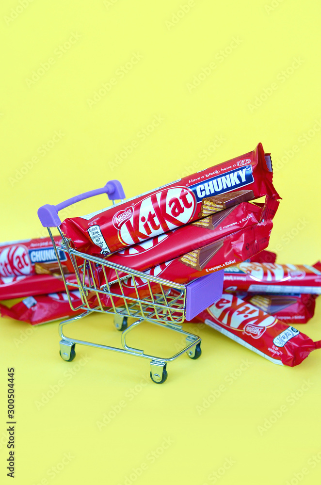 Kit Kat chocolate bars in small shopping cart on yellow background. Kit ...