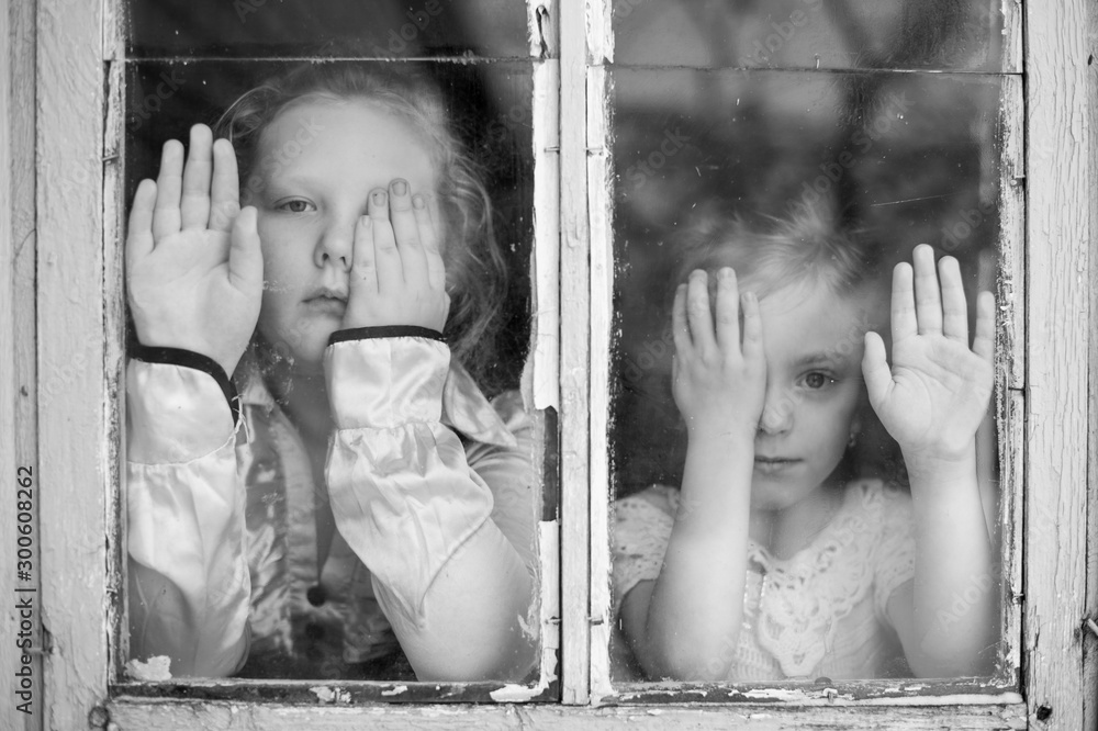 Two little girls covering their eye with a hand and looking at window ...