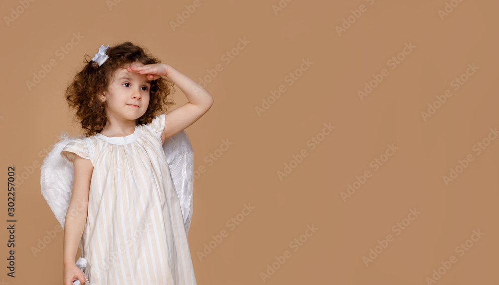 Little curly Angel girl with wings and dress seeking at side. beige at ...