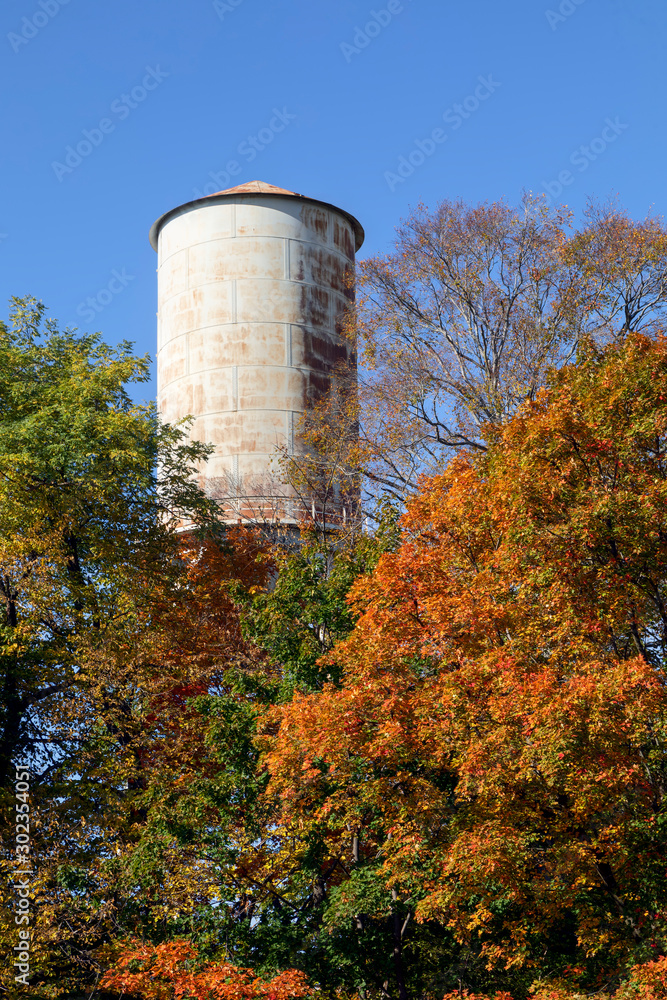 An old water tower rises above trees displaying beautiful fall foliage ...