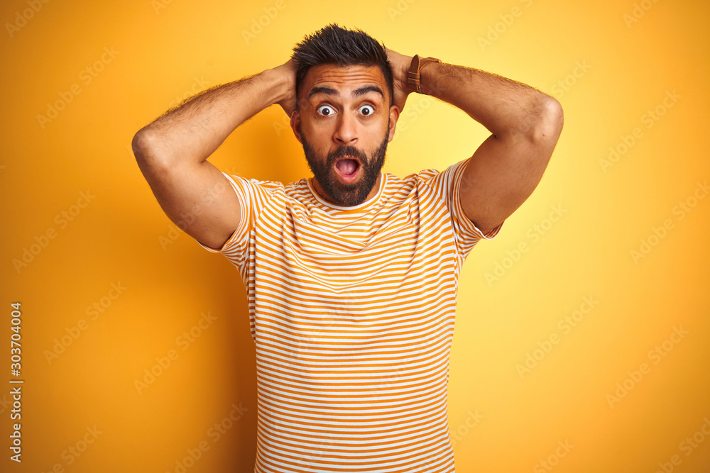 Young indian man wearing t-shirt standing over isolated yellow ...