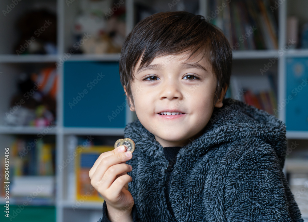 Portrait of Happy kid wearing fulffy pyjamas holding two pound coins ...