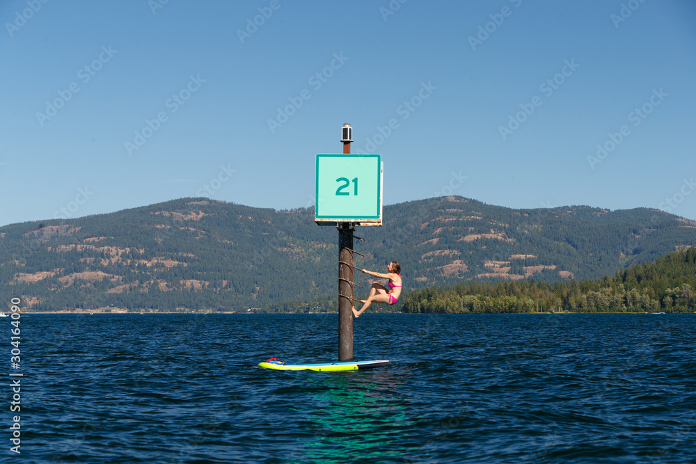 A woman in a bathing suit climbs a buey while SUPing in Lake Pend ...