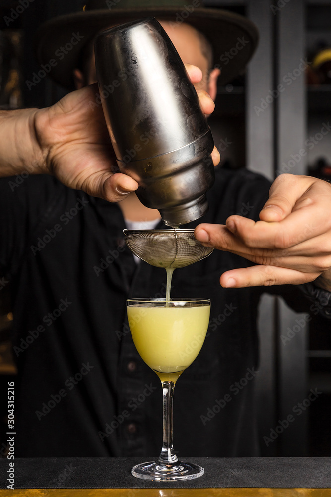 Bartender pouring a drink from a shaker through a strainer into a ...