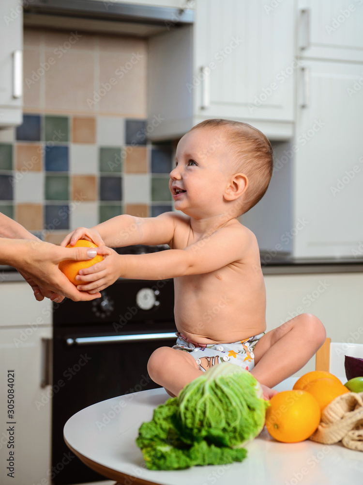 Cute baby boy at the table with fruits and vegetables. Feeding child ...