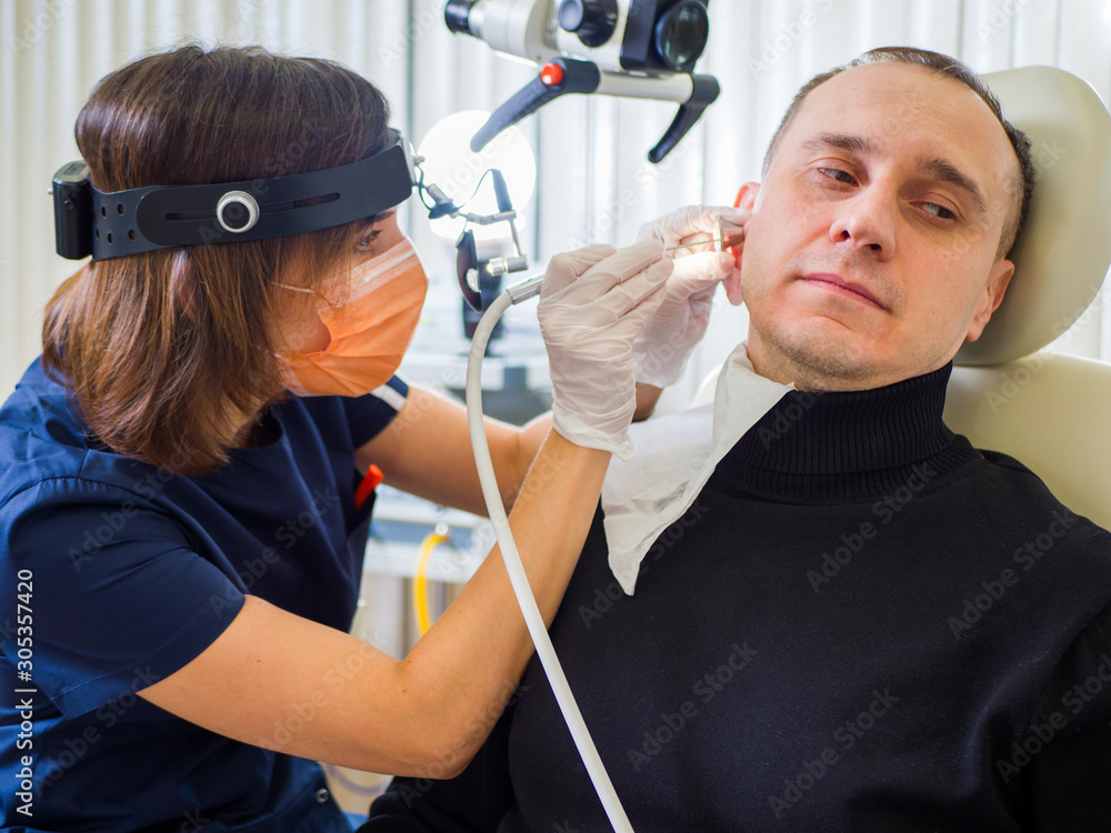 Female doctor cleans the ear of a patient to a man. ENT clinic scene ...