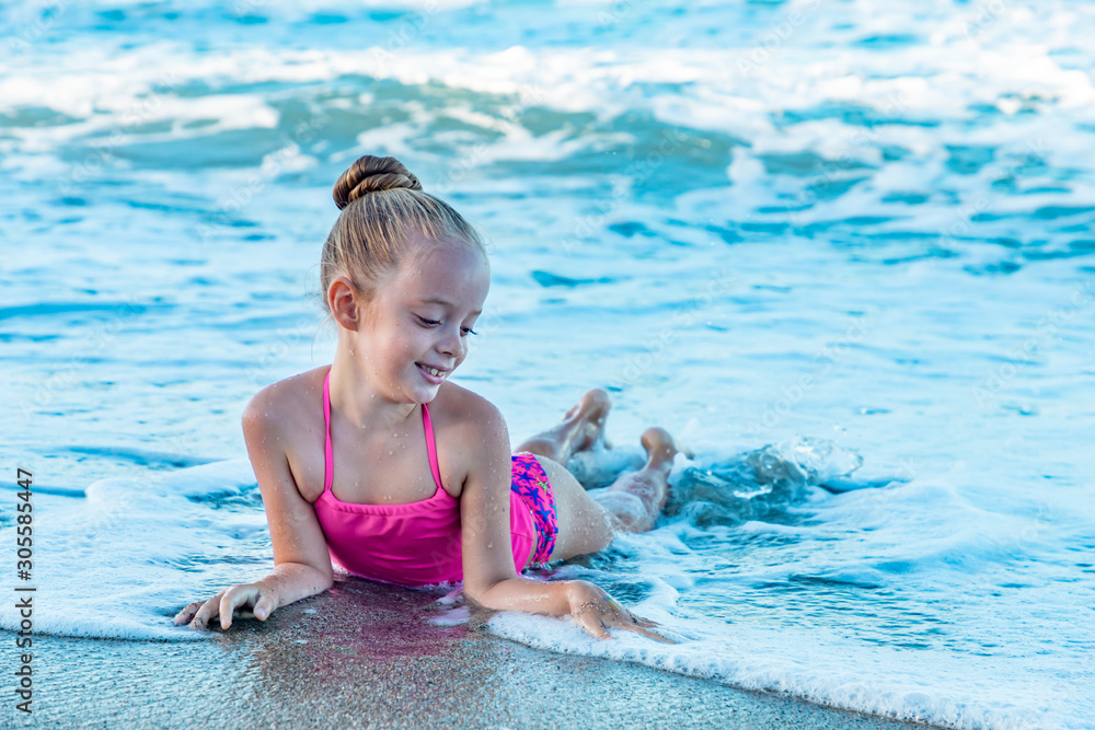 A playful smiling cute little girl in a colorful pink swimsuit lying in ...