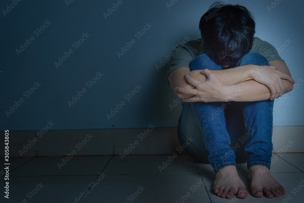sad man hug his knee and cry sitting alone in a dark room. Depression ...