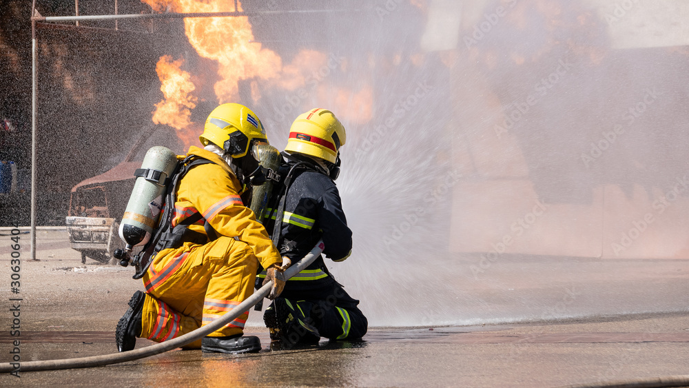 The back view of two firefighters practicing using fire-fighting water ...