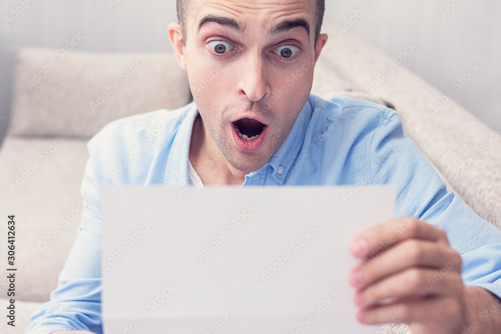 Shocked man reading a letter sitting on sofa at home, copy space, toned ...