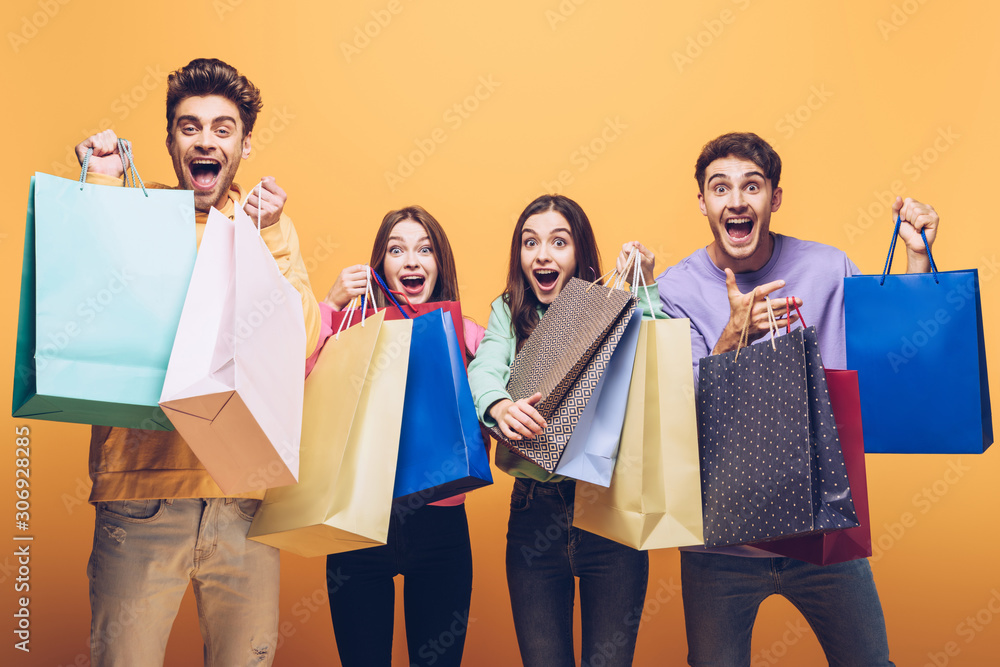 excited young friends shouting and holding shopping bags together ...