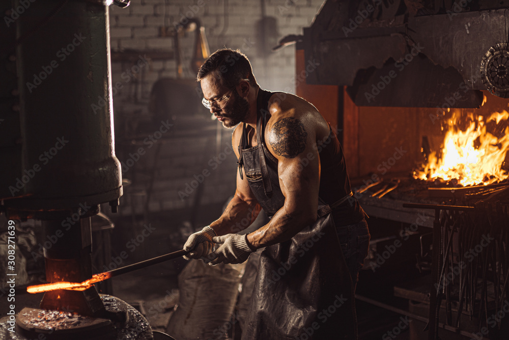Young forger shaping metal on a jackhammer in the blacksmith workshop ...