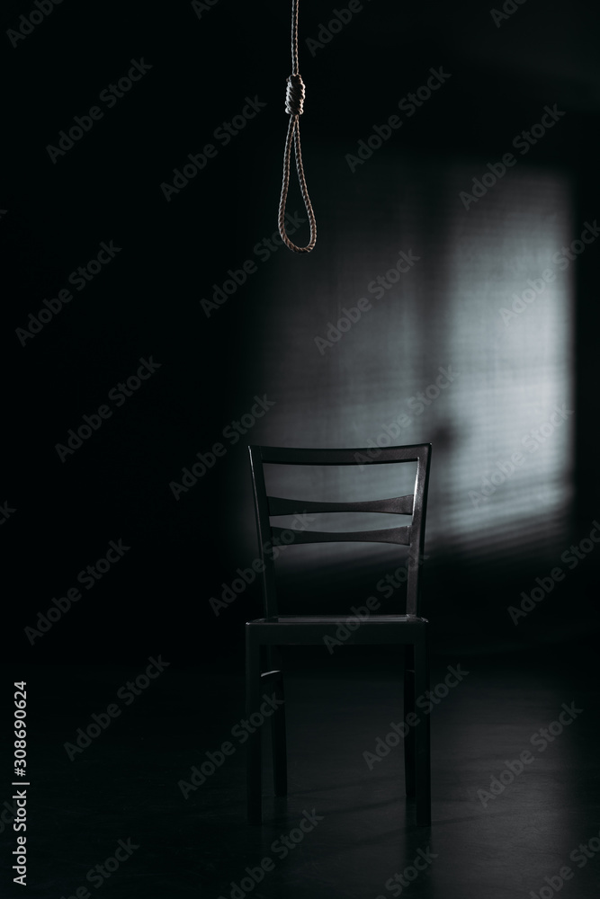 chair under hanging rope noose on black background with lighting ...