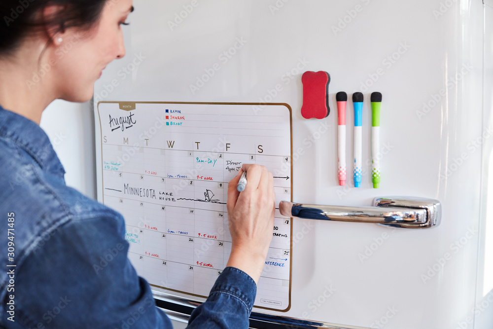 Woman filling out calendar on fridge Stock Photo | Adobe Stock