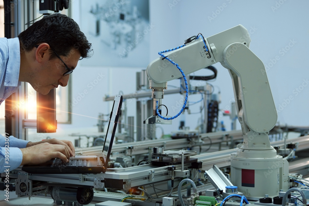 Close-up robot arm. Engineer is working on laptop to programming smart factory automation and ...