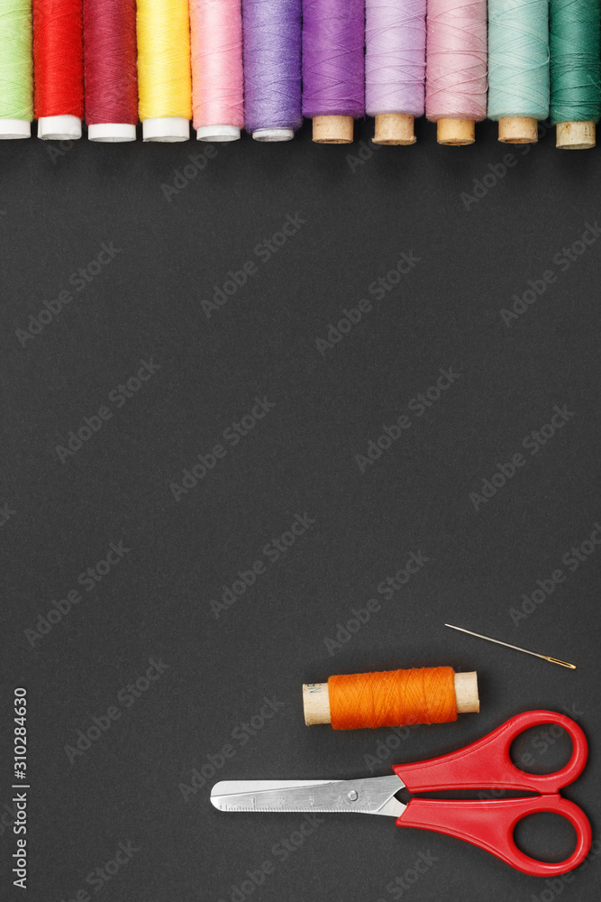 Colored thread coils, scissors and needle on a black background. The ...