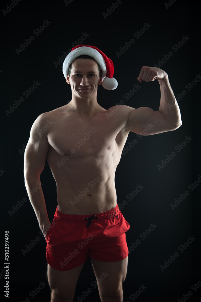 Feel my power. Muscular man wear santa claus hat. Bodybuilder on black ...