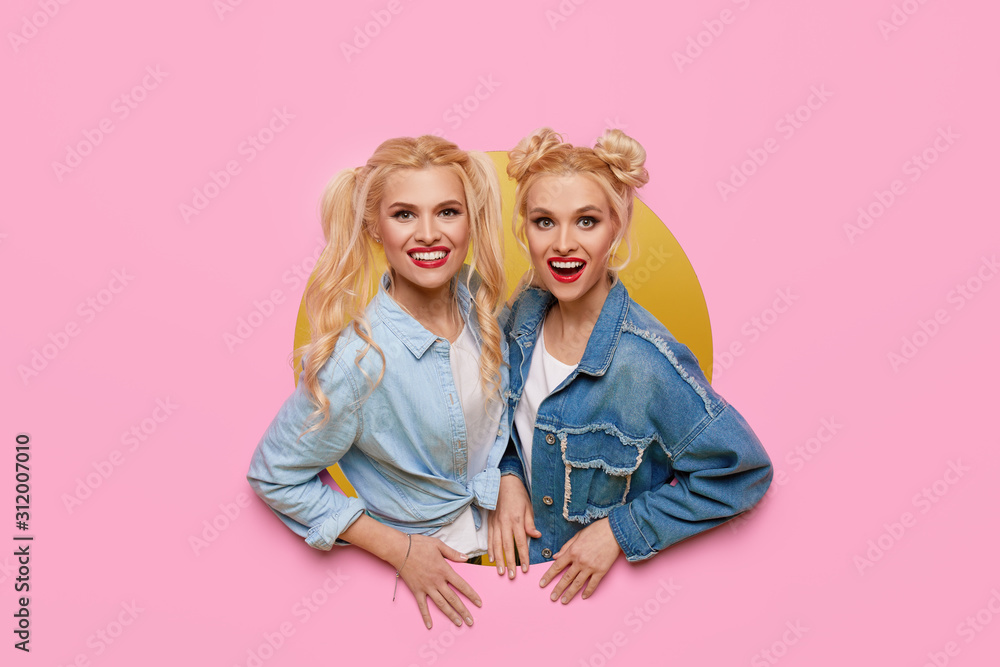 Image of two young happy shoked girlfriends women standing over pink ...