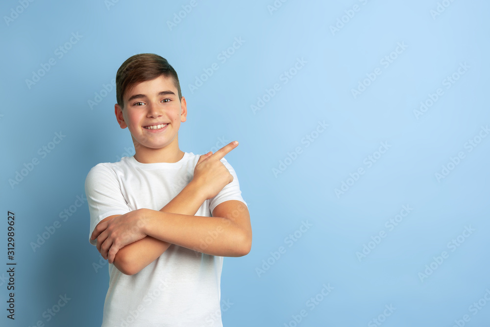 Smiling, pointing at side. Caucasian boy portrait isolated on blue ...
