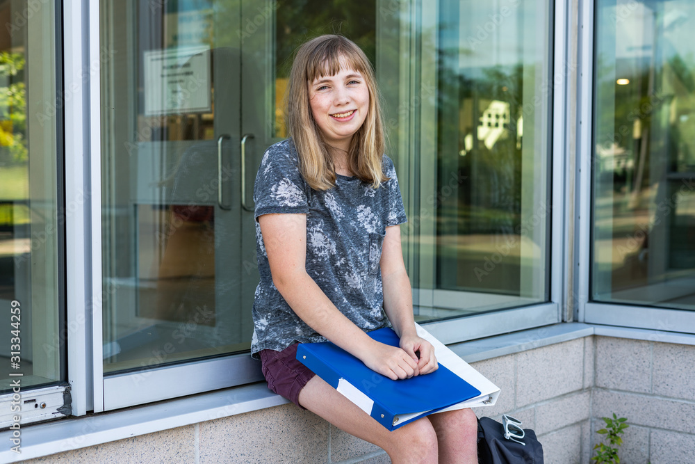 Happy/smiling teen girl/student sitting on a window ledge of her school ...