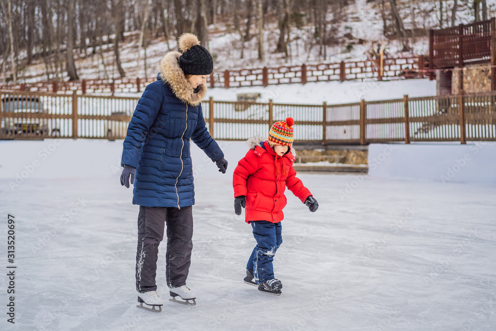 young mother teaching her little son ice skating at outdoor skating ...