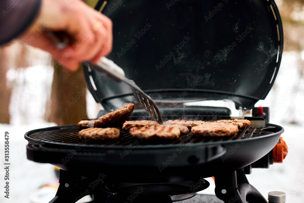 Man grilling steaks on a portable BBQ, Snowy winter barbecue outdoors ...