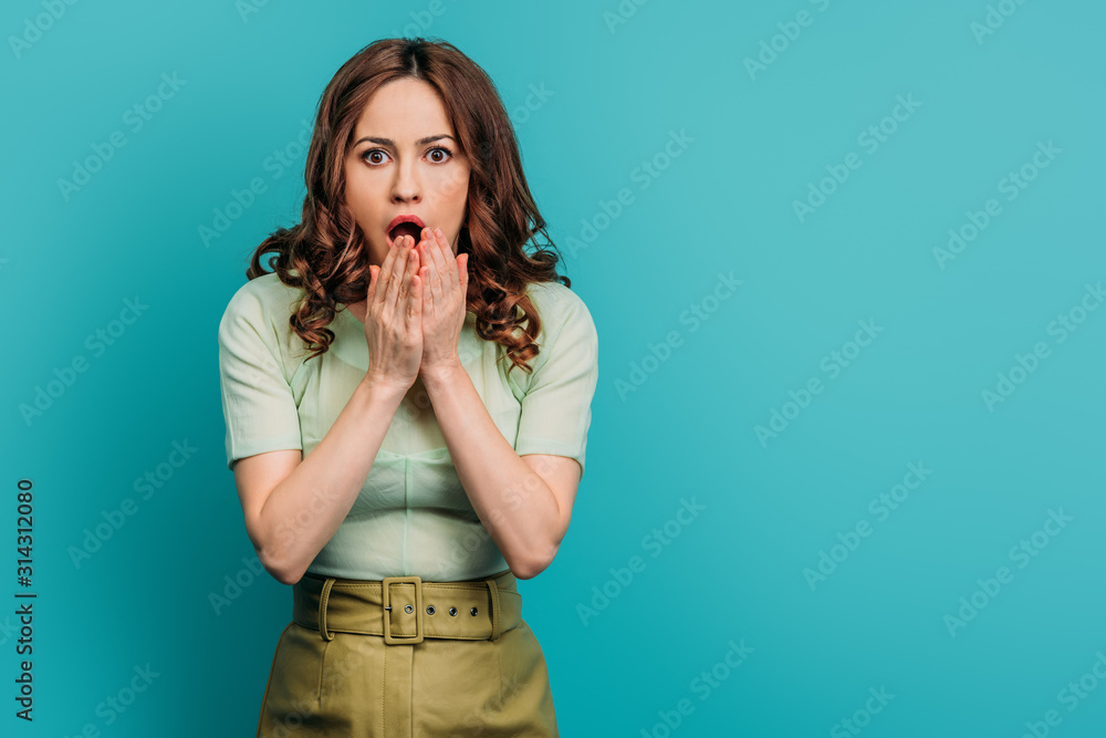 shocked woman holding hands near face while standing with open mouth on ...