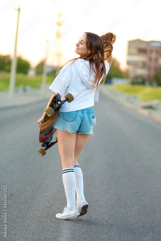 Street portrait of a girl in casual clothes and longboard in her hand ...