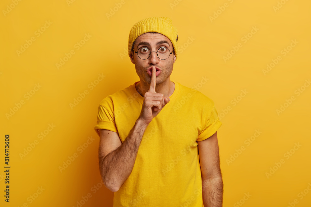 Surprised adult man keeps gossip, stands silent and quiet, holds index ...