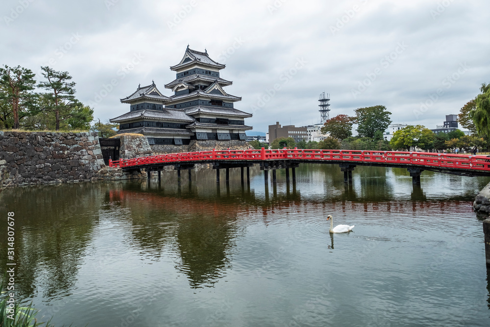 Matsumoto castle with red bridge and it’s reflection over water against ...