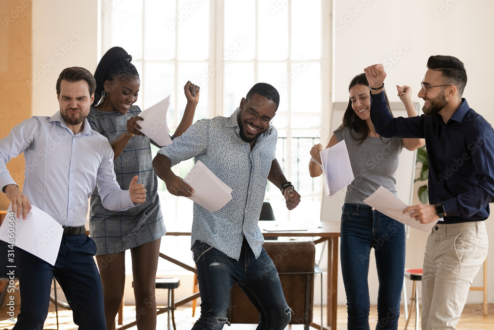 Overjoyed multiethnic employees dancing at workplace celebrating work ...
