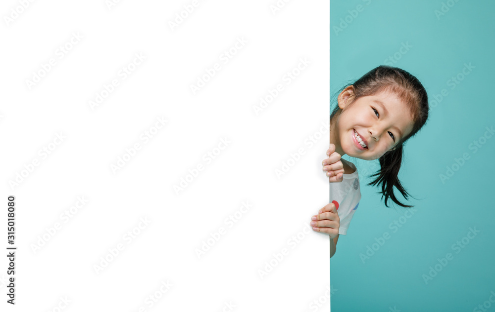 Smiling happy cute child hiding behind a blank white board, empty space ...