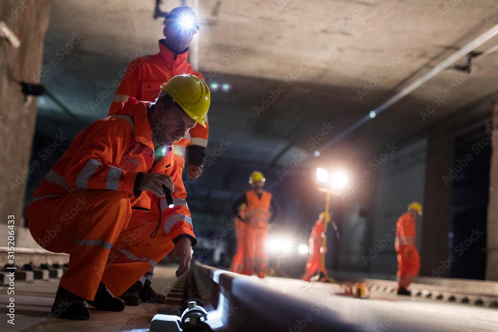 Male construction workers examining underground tracks at dark ...