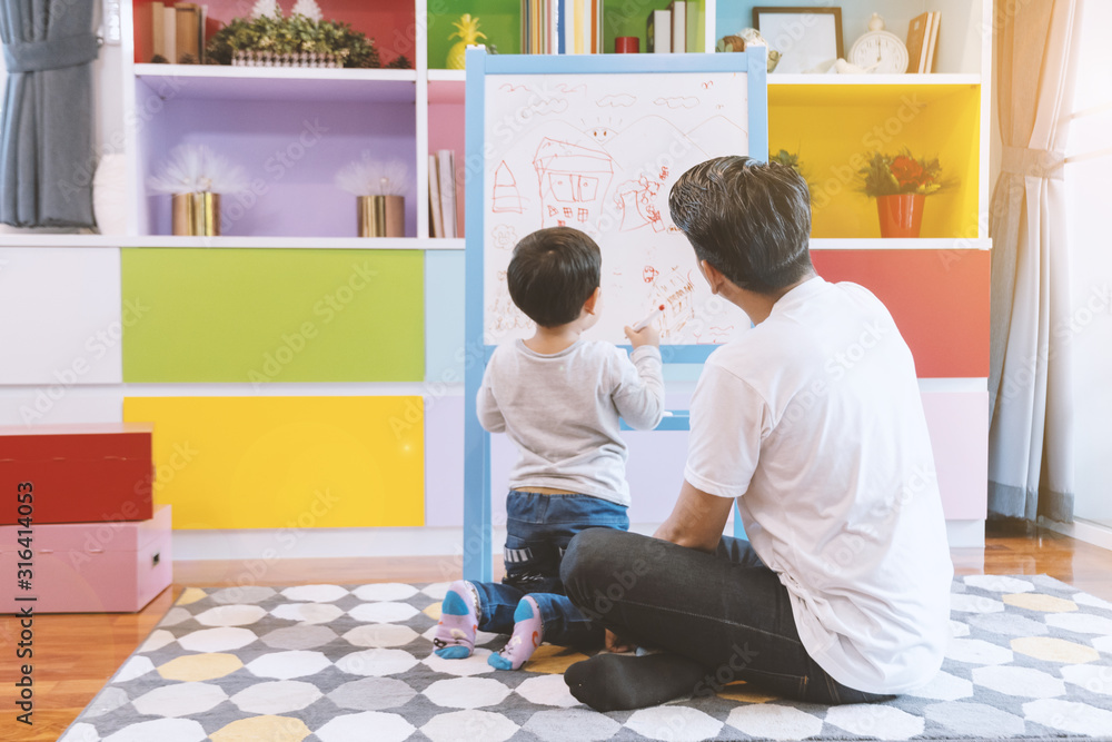 Happy cute little boy and father drawing a house with pen on whiteboard ...