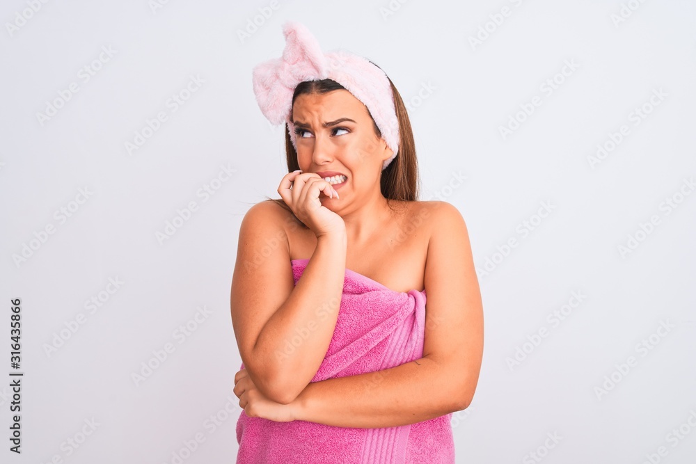 Beautiful young woman wearing pink shower towel and beauty headband over white background ...
