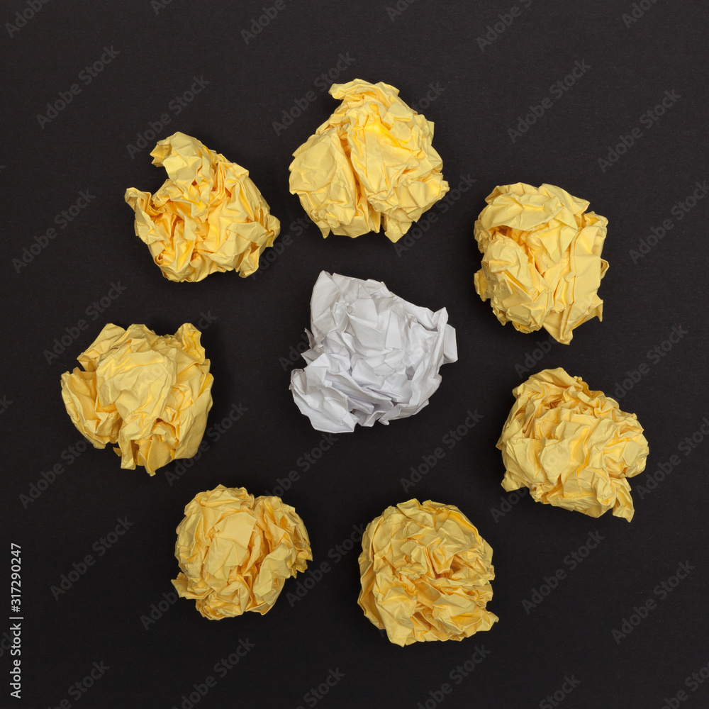 Crumpled white paper ball in the center of yellow balls on a black ...