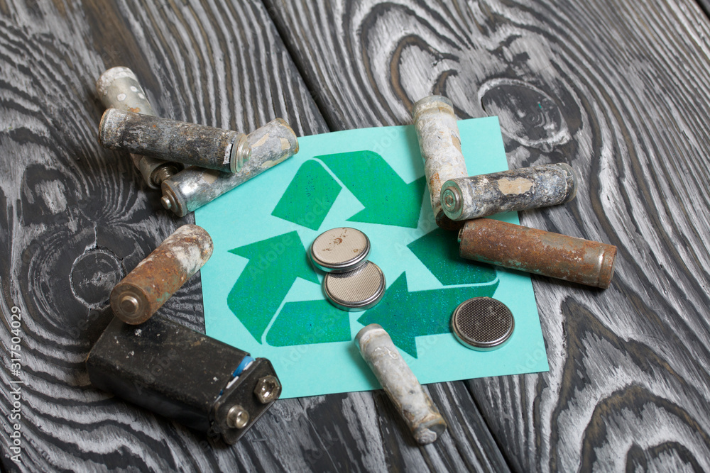 Spent finger-type batteries coated with corrosion. Waste recycling sign. They lie on brushed ...