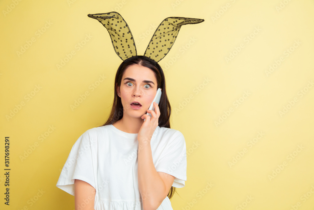 Shocked talking on phone. Caucasian woman as an Easter bunny on yellow ...